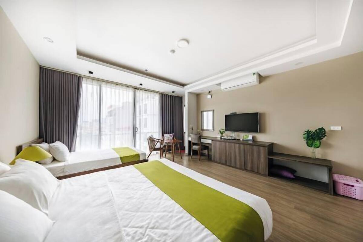 Quarto de hotel com duas camas, uma escrivaninha, televisão e uma janela grande com cortinas.