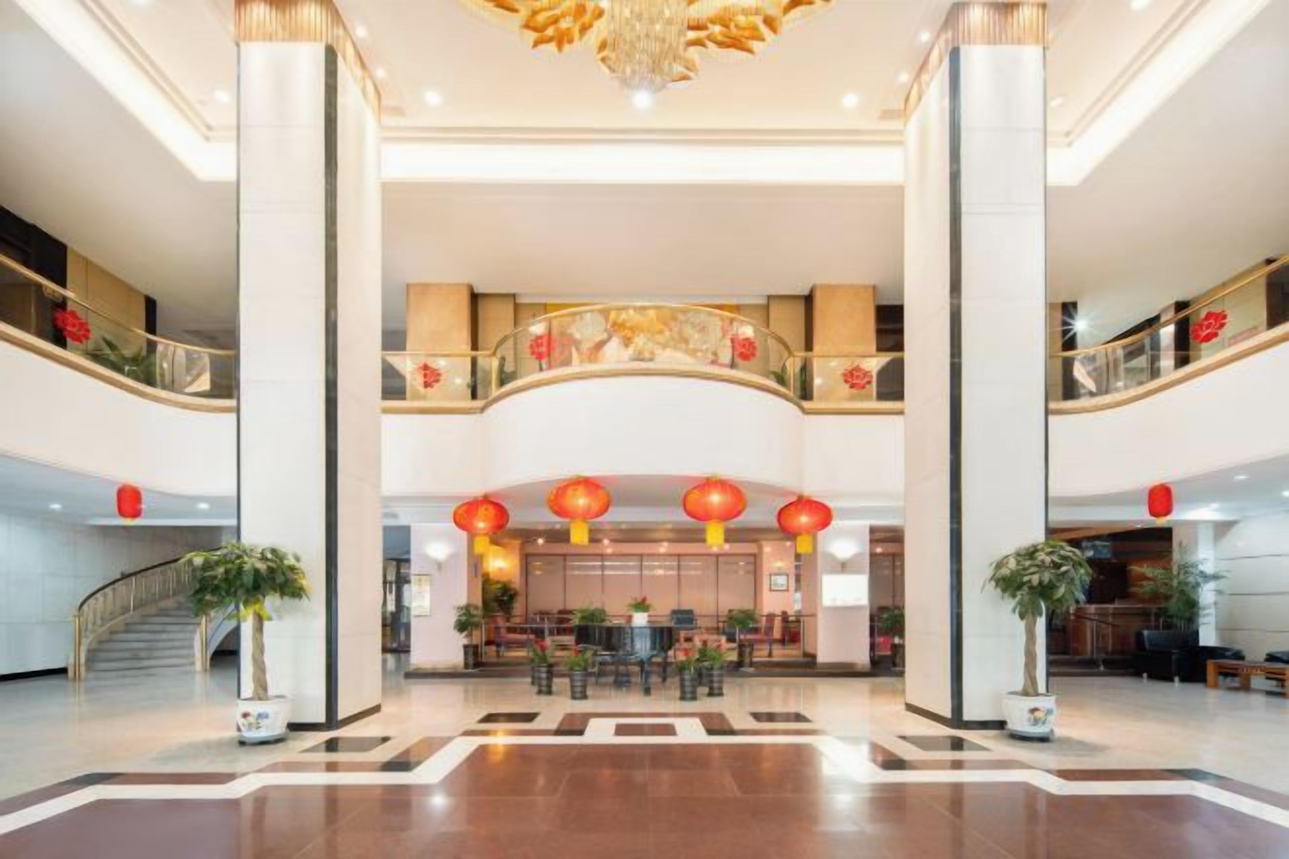 Um hall amplo com área de estar central, escada e um grande lustre.