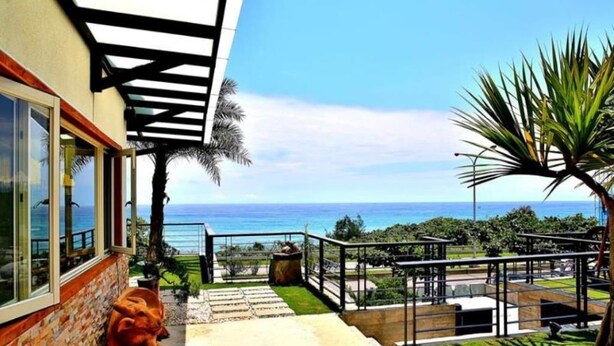 Um imóvel à beira-mar com varanda, vista para o oceano e escadaria de pedra até um deck.