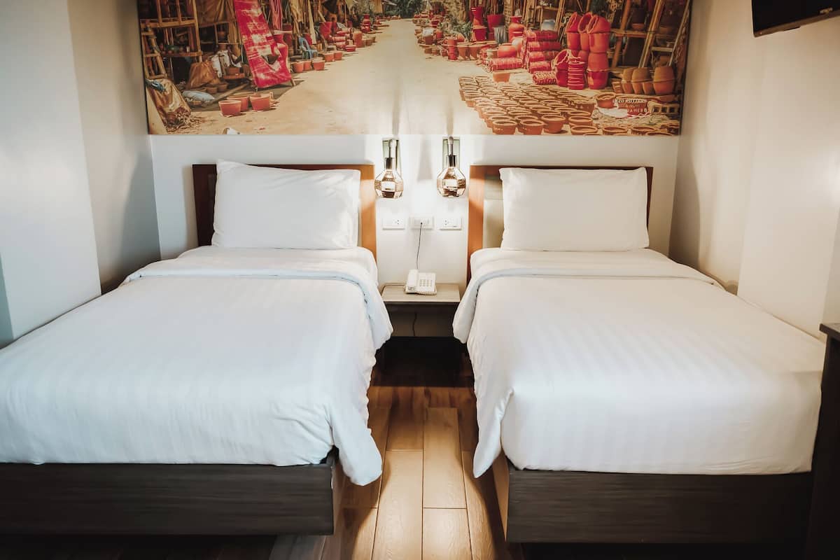Quarto duplo com duas camas, piso de madeira, telefone fixado na parede e um mural sobre as camas.