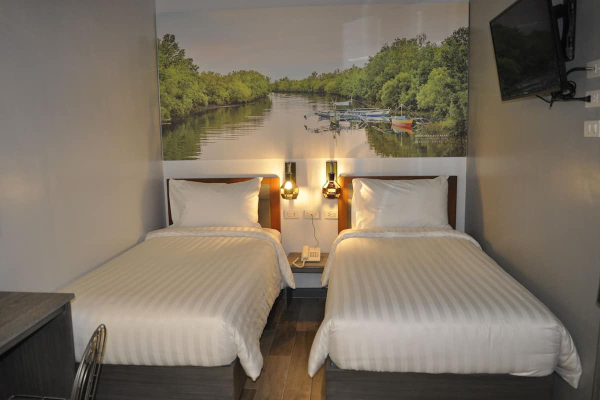 Quarto de hotel com duas camas, uma escrivaninha e uma janela grande com vista para um rio e barcos.