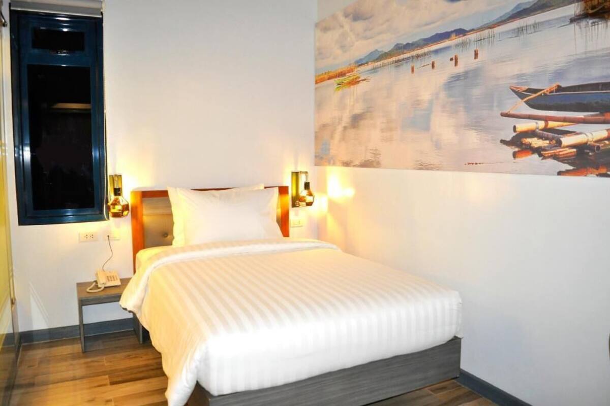 Quarto de hotel com cama, luminárias de cabeceira, mesa de cabeceira com telefone e um quadro de uma ponte sobre a água na parede.