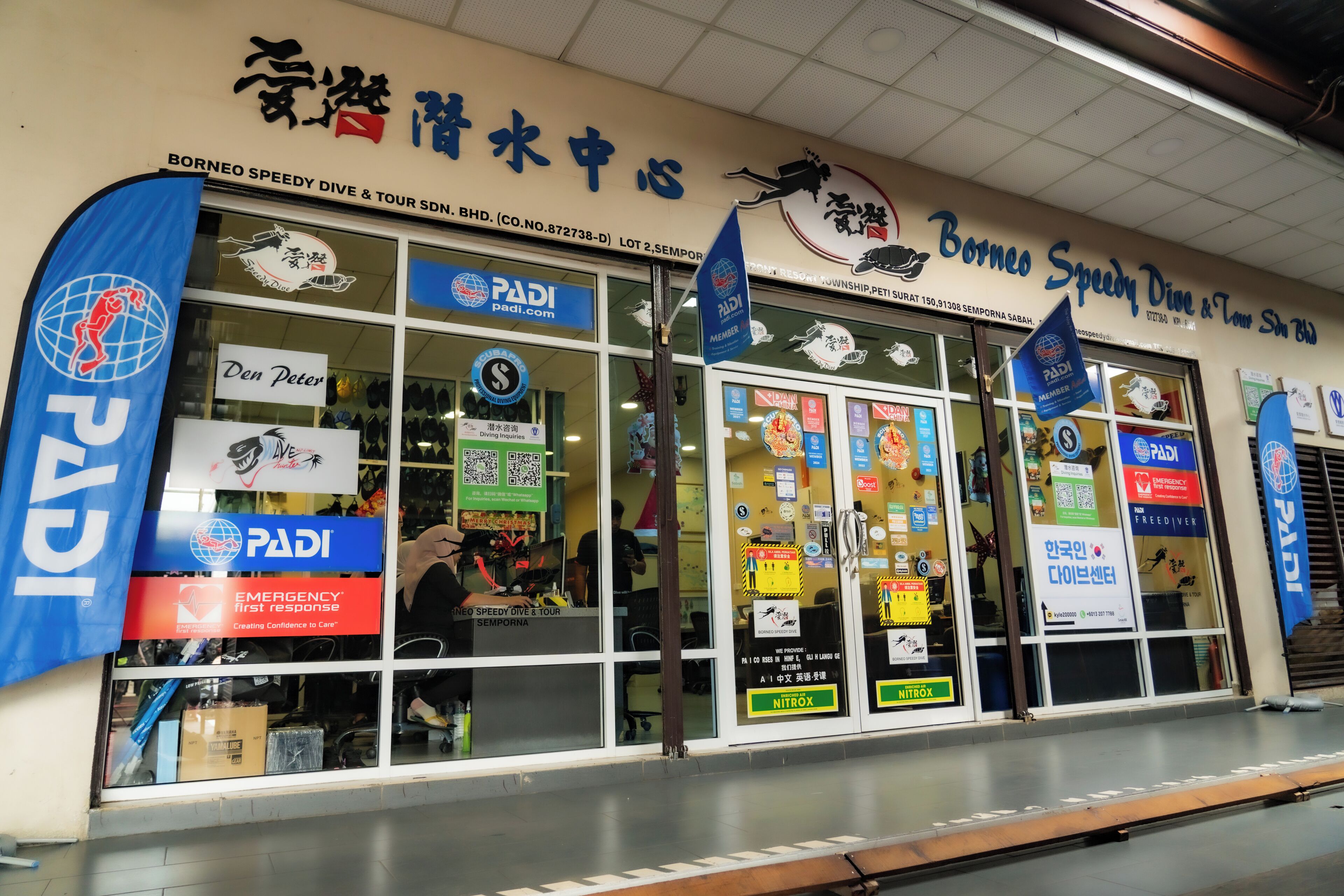 Vitrine com grandes janelas exibindo diversos artigos e uma placa indicando Borneo Speedy Dive & Tour SDN. BHD.