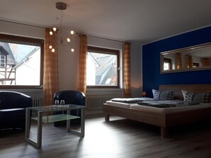 Quarto moderno com cama, mesa de vidro, uma cadeira e uma janela grande com cortinas.