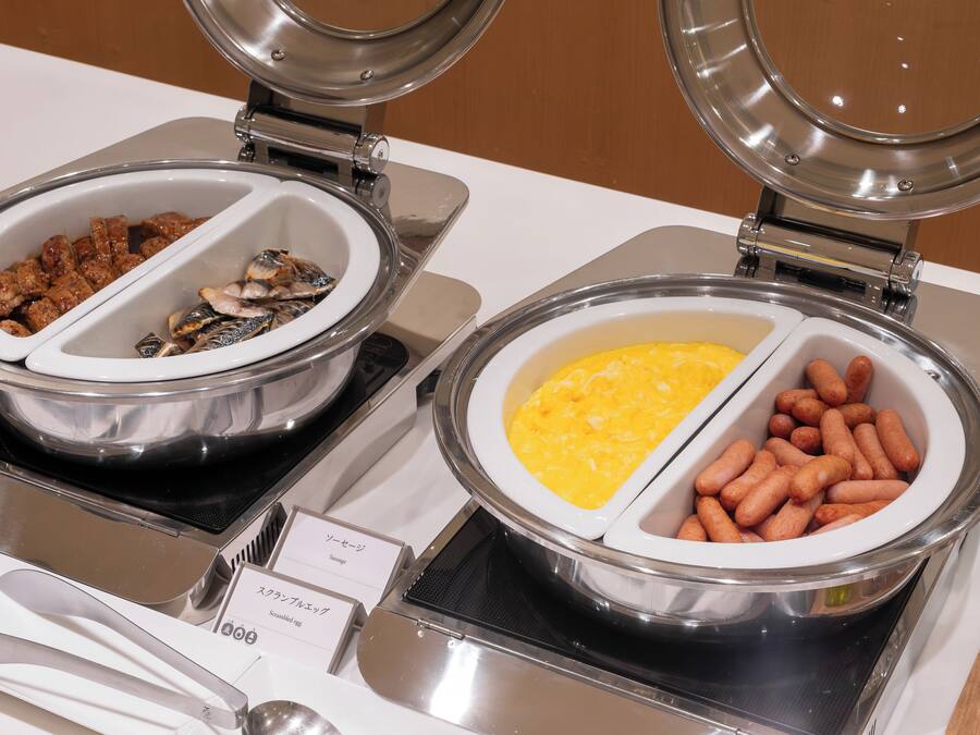 Buffet com duas travessas de ovos mexidos e salsichas, e outra com ovos mexidos e camarões.