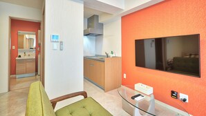 Quarto de hotel moderno com cozinha compacta, mesa de centro de vidro, televisão de tela plana e sofá.