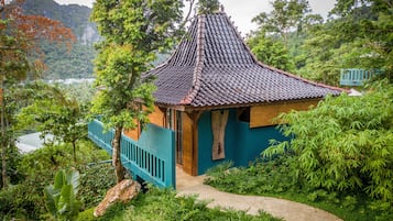 Uma casa tradicional com telhado de telhas, rodeada por vegetação exuberante e vista para um lago.