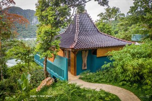 Uma casa tradicional com telhado de telhas, rodeada por vegetação exuberante e vista para um lago.