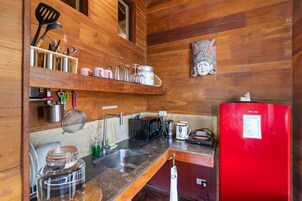 Cozinha compacta com paredes de madeira, geladeira vermelha, pia de aço inoxidável e diversos utensílios de cozinha nas prateleiras.