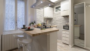 Uma cozinha moderna com ilha central, armários brancos e uma janela com cortinas estampadas.