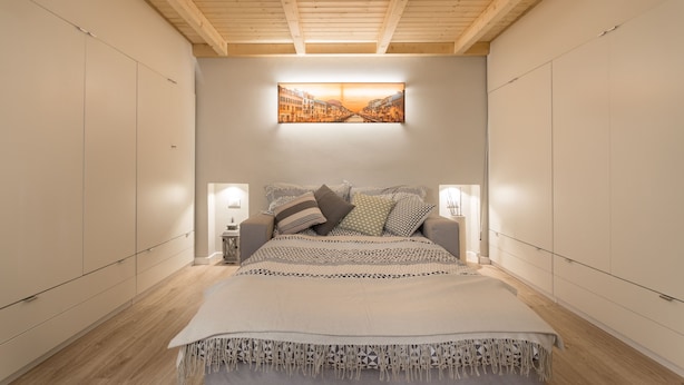 Quarto com cama, mesa de cabeceira, obra de arte na parede e armários embutidos.