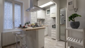Uma cozinha moderna com ilha central, armários brancos, forno embutido e janela com cortinas estampadas.