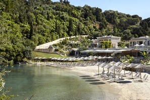 Um resort à beira-mar com espreguiçadeiras e guarda-sóis, piscina e edifícios com fachadas de pedra.