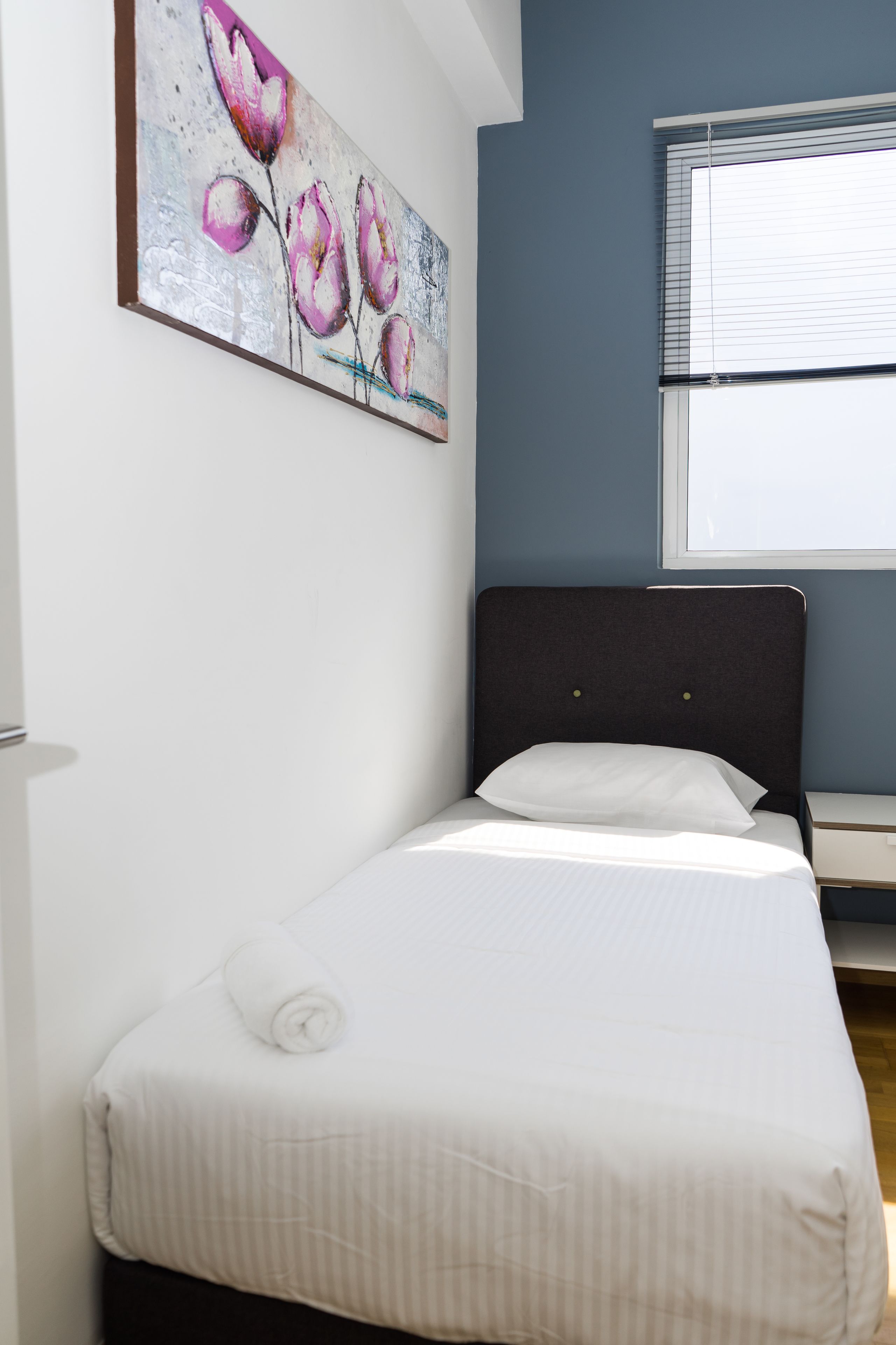 Quarto com cama, mesa de cabeceira, janela com persianas e um quadro na parede.