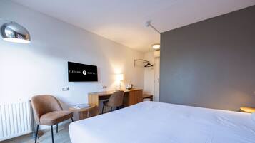Quarto de hotel com cama, escrivaninha, cadeira, televisão e radiador.