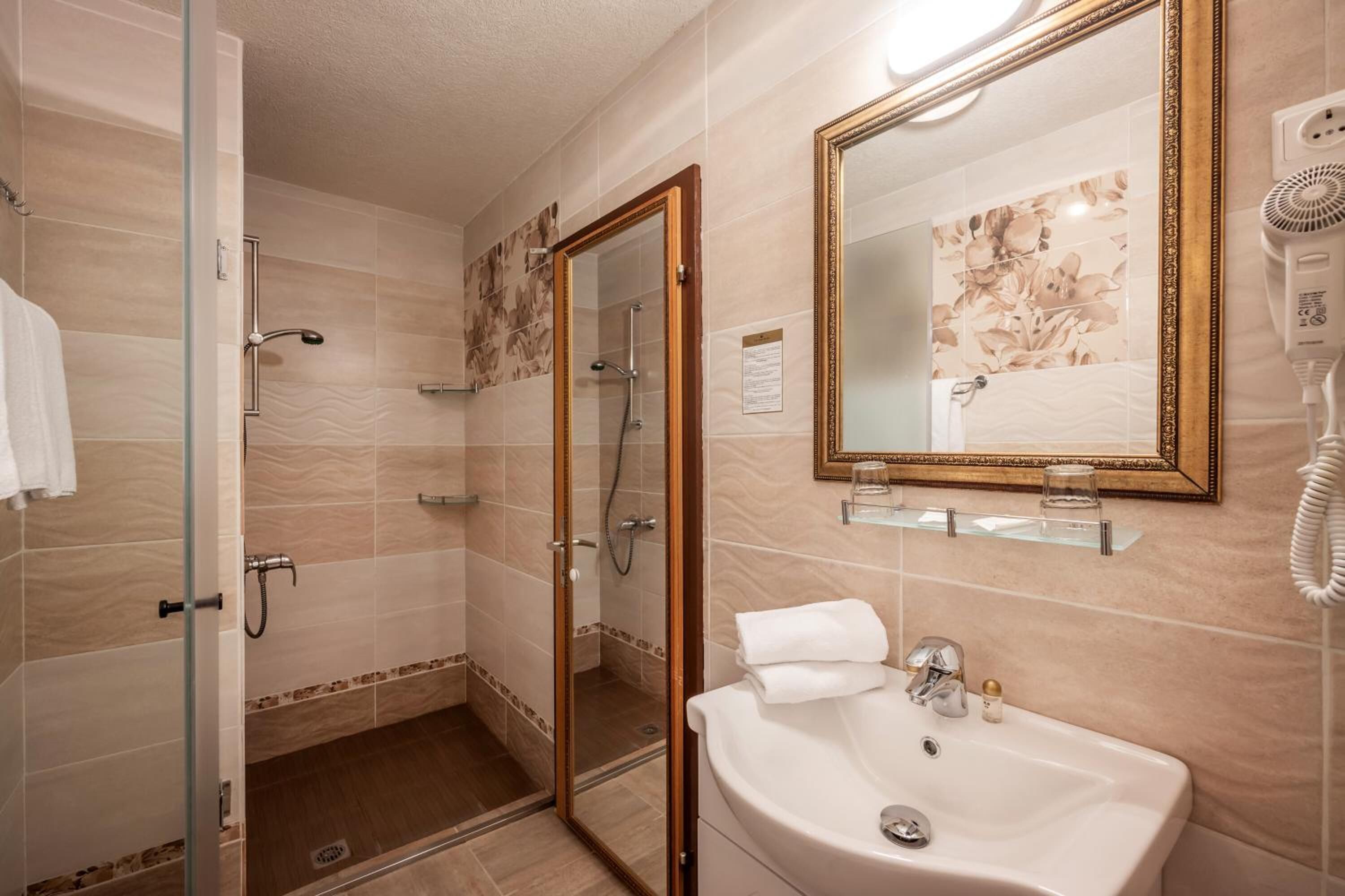 Casa de banho com cabine de duche em vidro, lavatório com espelho e secador de cabelo na parede.