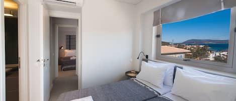 Quarto de hotel com cama, mesa de cabeceira, janela e vista para o mar, e um aparelho de ar condicionado.