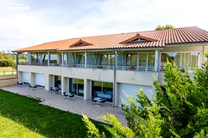 Um edifício de dois andares com telhado de telhas vermelhas, janelas amplas e área de estar ao ar livre.