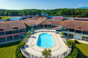 Piscina rodeada por edifícios com telhados em tijolos vermelhos, uma área de estar coberta e vista para uma área arborizada.