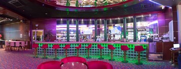 Uma área de bar com balcão, várias telas e banquetas vermelhas.