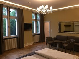 Quarto de hotel com cama, televisão, lustre, sofá e mesa de jantar.