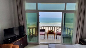 Quarto de hotel com varanda ampla, televisão, cama e mesa com frutas.