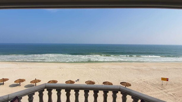 Vista da praia a partir de uma varanda com grades, mar e guarda-sóis.