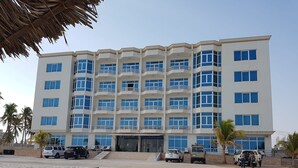 Hotel de vários andares com varandas, localização à beira-mar e vários veículos estacionados em frente.
