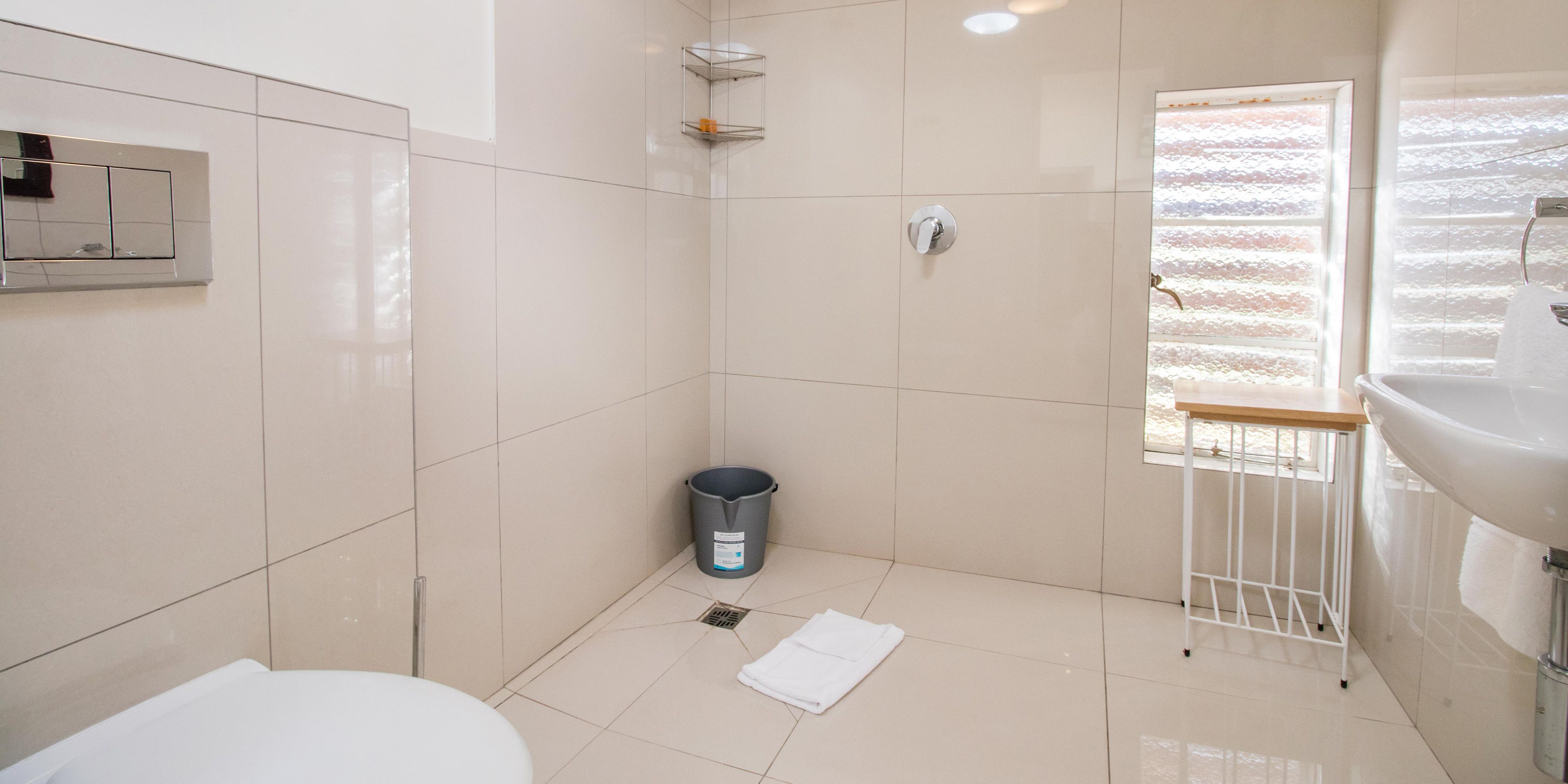 Casa de banho com sanita, zona de duche, lavatório e janela com estores.