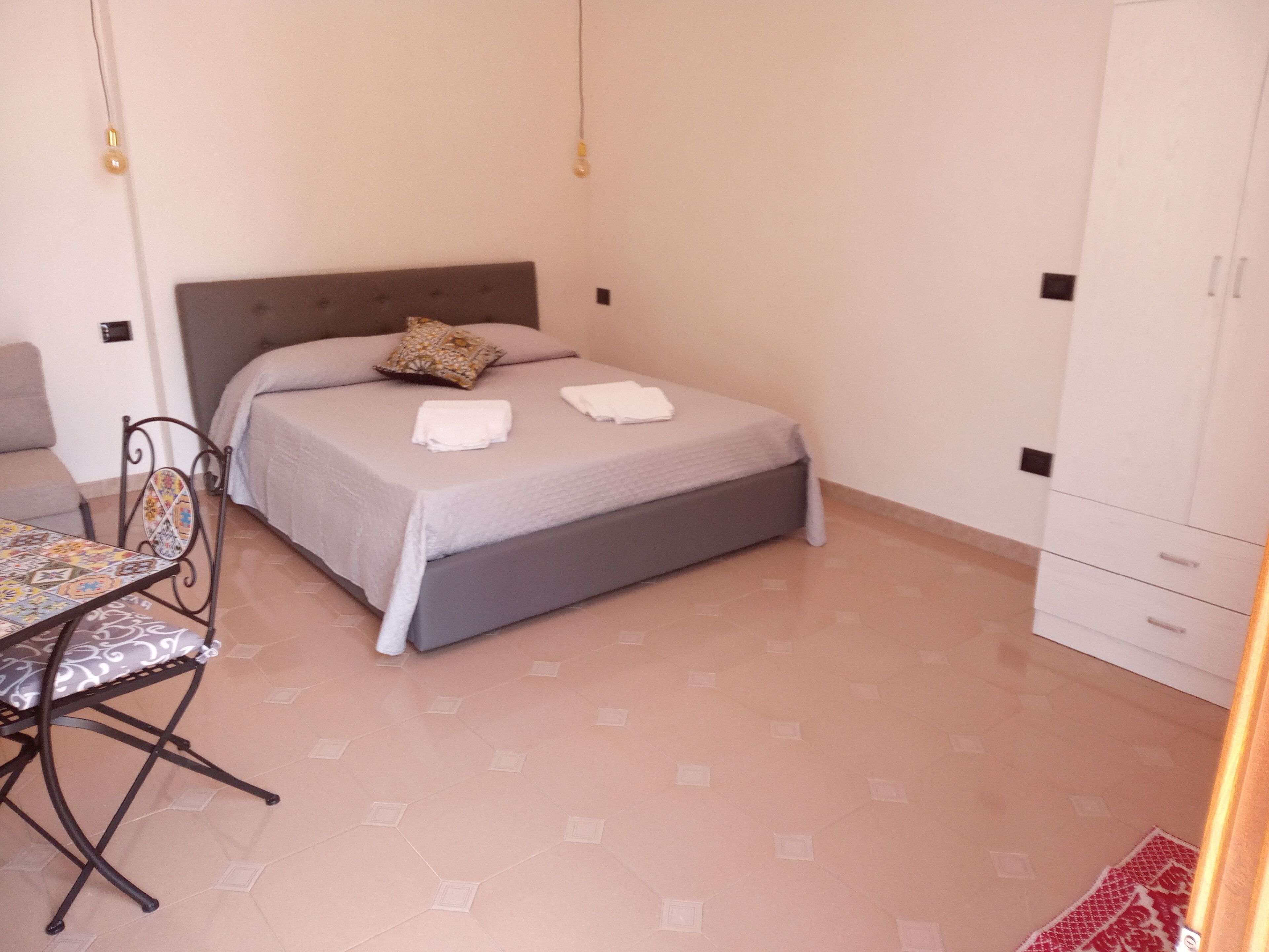 Um quarto com cama, cadeira, guarda-roupa e mesa.