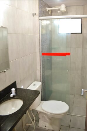 Casa de banho com sanita, lavatório e cabine de duche de vidro.