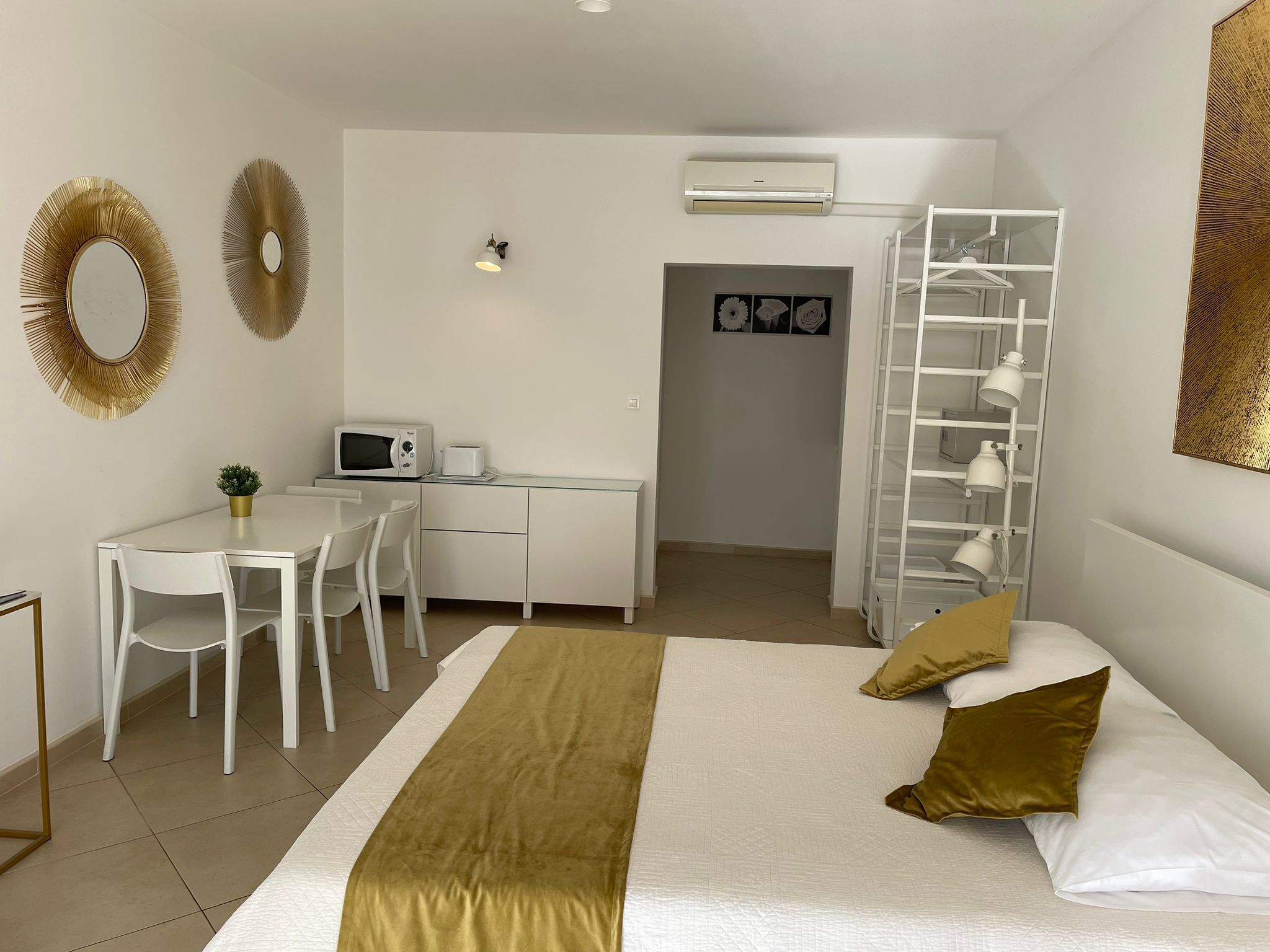 Quarto de hotel pequeno, com uma cama, escrivaninha, cadeira, pequena mesa com uma planta e guarda-roupa com espelho.