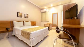 Quarto de hotel com uma cama, uma escrivaninha, uma cadeira, telefone, televisão e espelho.