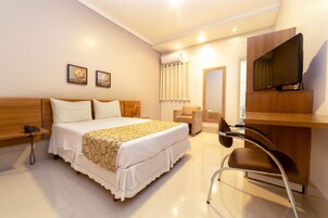 Quarto de hotel com uma cama, uma escrivaninha, uma cadeira, telefone, televisão e espelho.