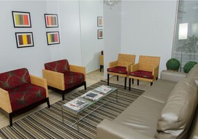 Uma sala de estar com móveis de vime, tapete listrado e quadros nas paredes.