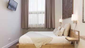 Quarto bem arrumado com cama, luminárias de cabeceira, televisão fixada na parede e um objeto decorativo.