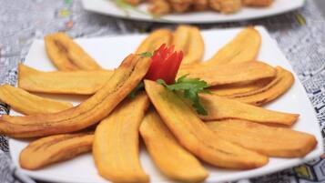 Um prato de banana da terra frita, decorado com uma fatia de tomate e salsa.
