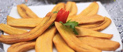 Um prato de banana da terra frita, decorado com uma fatia de tomate e salsa.