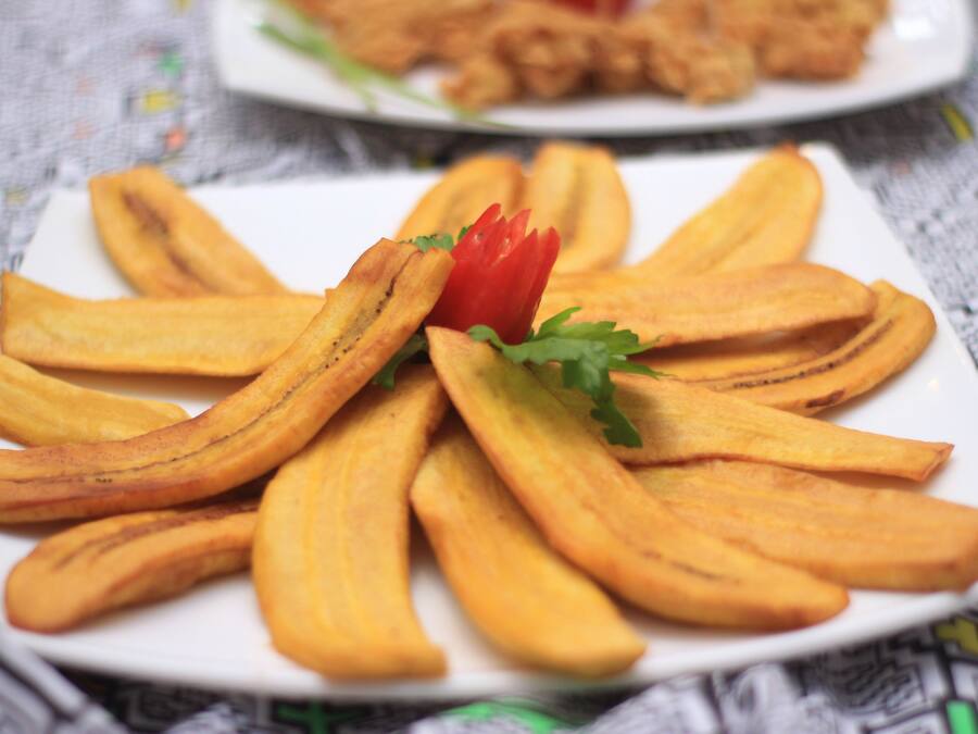 Um prato de banana da terra frita, decorado com uma fatia de tomate e salsa.