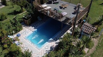 Vista aérea de uma área de piscina com deck, espreguiçadeiras e um pequeno jardim.