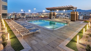 Uma área de piscina no terraço com espreguiçadeiras, uma pérgula e vista para a cidade.