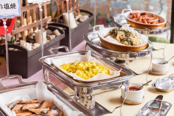Buffet com diversos pratos, incluindo ovos mexidos, linguiça e outros alimentos preparados.