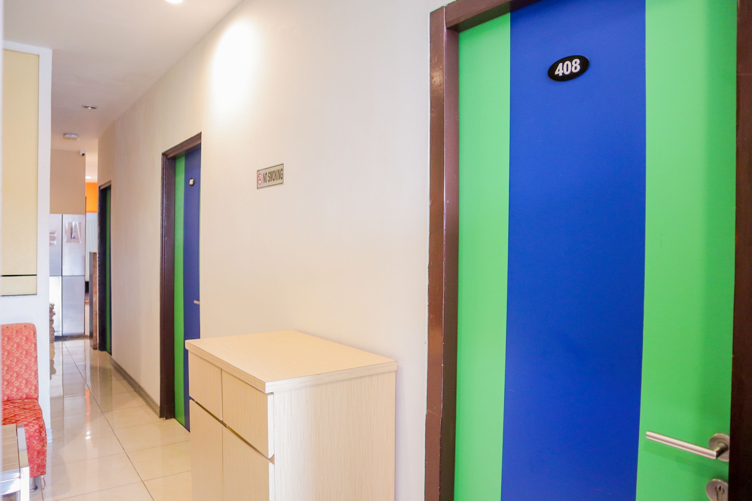 Um corredor com portas numeradas 408 e 409, um armário pequeno e uma cadeira vermelha.