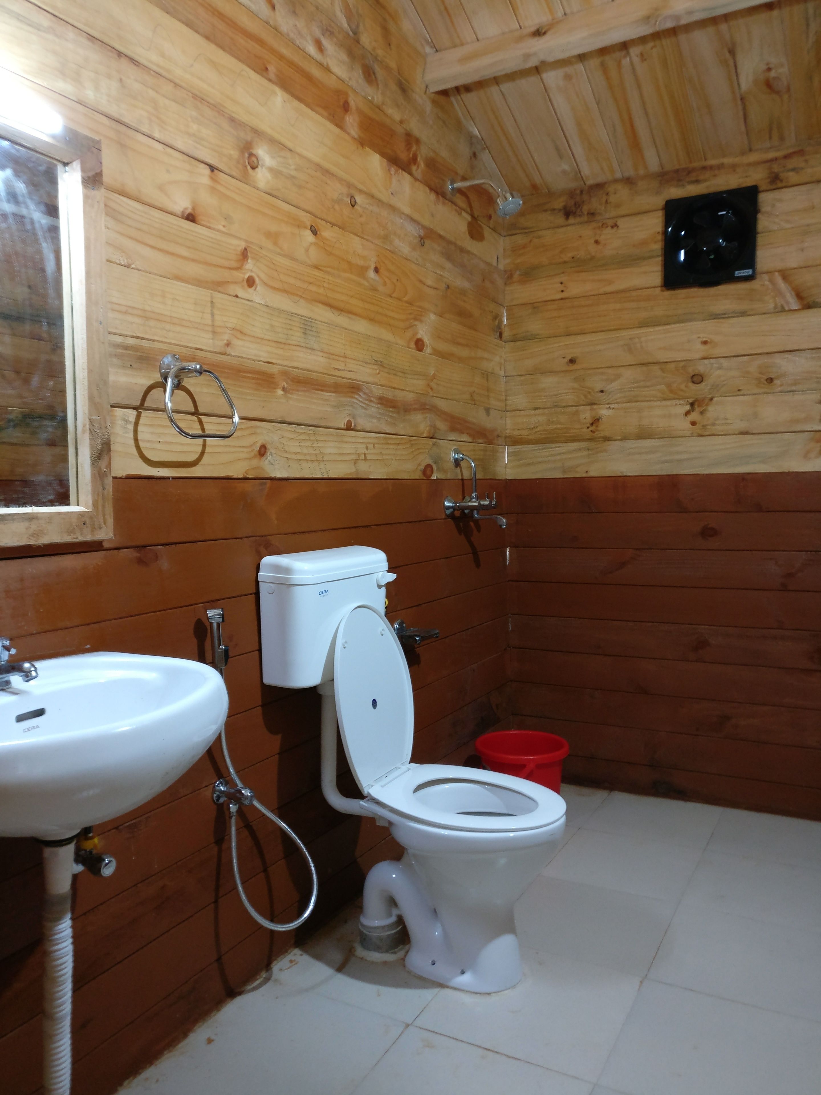 Casa de banho de uma cabana de madeira, com sanita branca, lavatório e chuveiro.