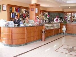 Uma área de recepção de hotel com balcão de madeira, um laptop e diversos objetos expostos.