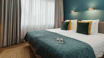 Quarto de hotel com uma cama grande, vista para o exterior através de cortinas leves e uma parede cor de verde-água.