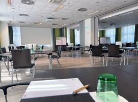 Sala de conferências com mesas, cadeiras, projetor e quadro branco.
