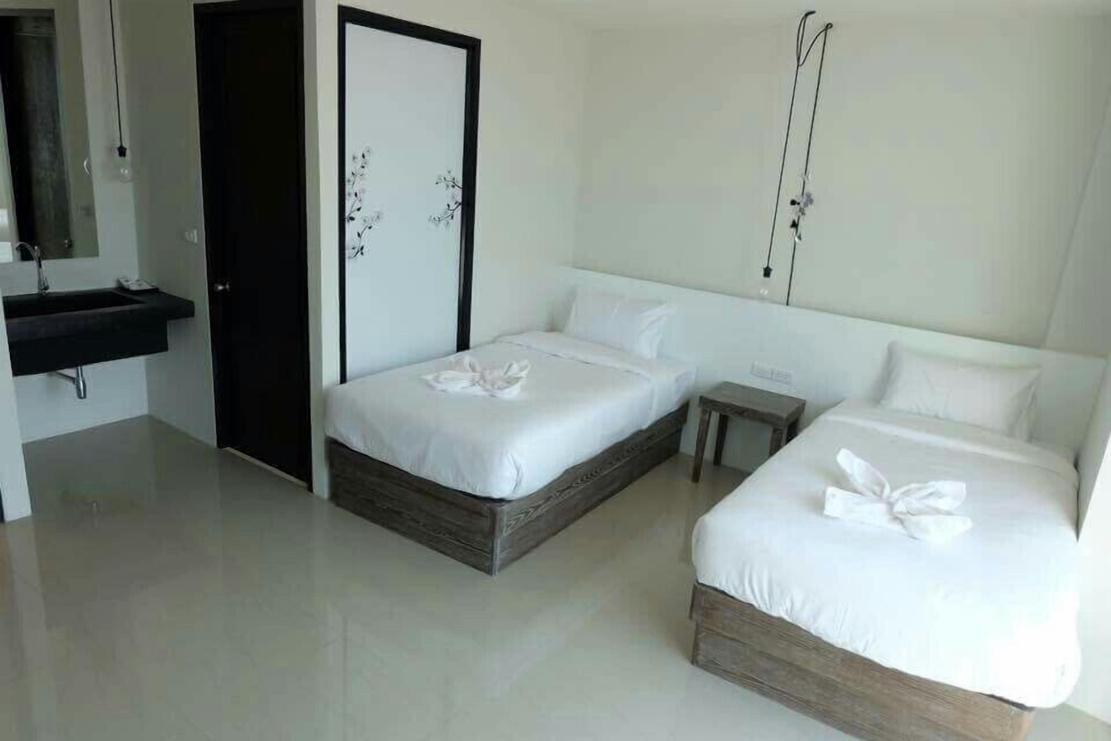 Quarto de hotel com duas camas, mesa de cabeceira, espelho e pia.