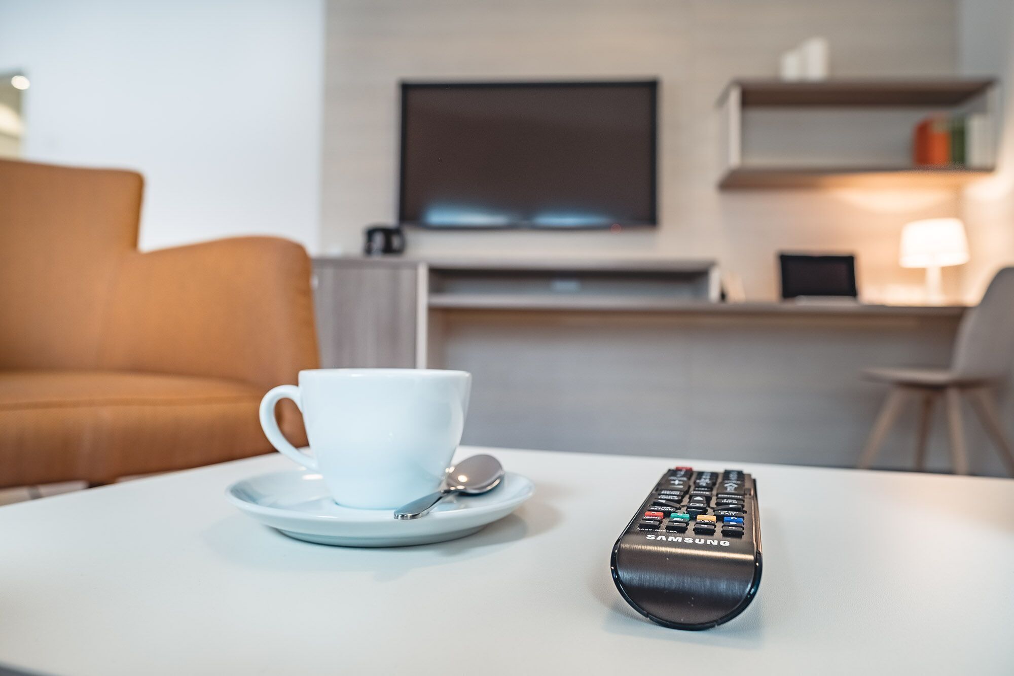 Um controle remoto e uma xícara sobre uma mesa num quarto de hotel.