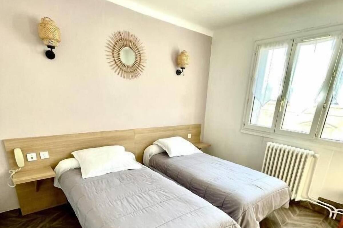 Quarto com duas camas, piso de madeira, janela e luminárias fixadas na parede.